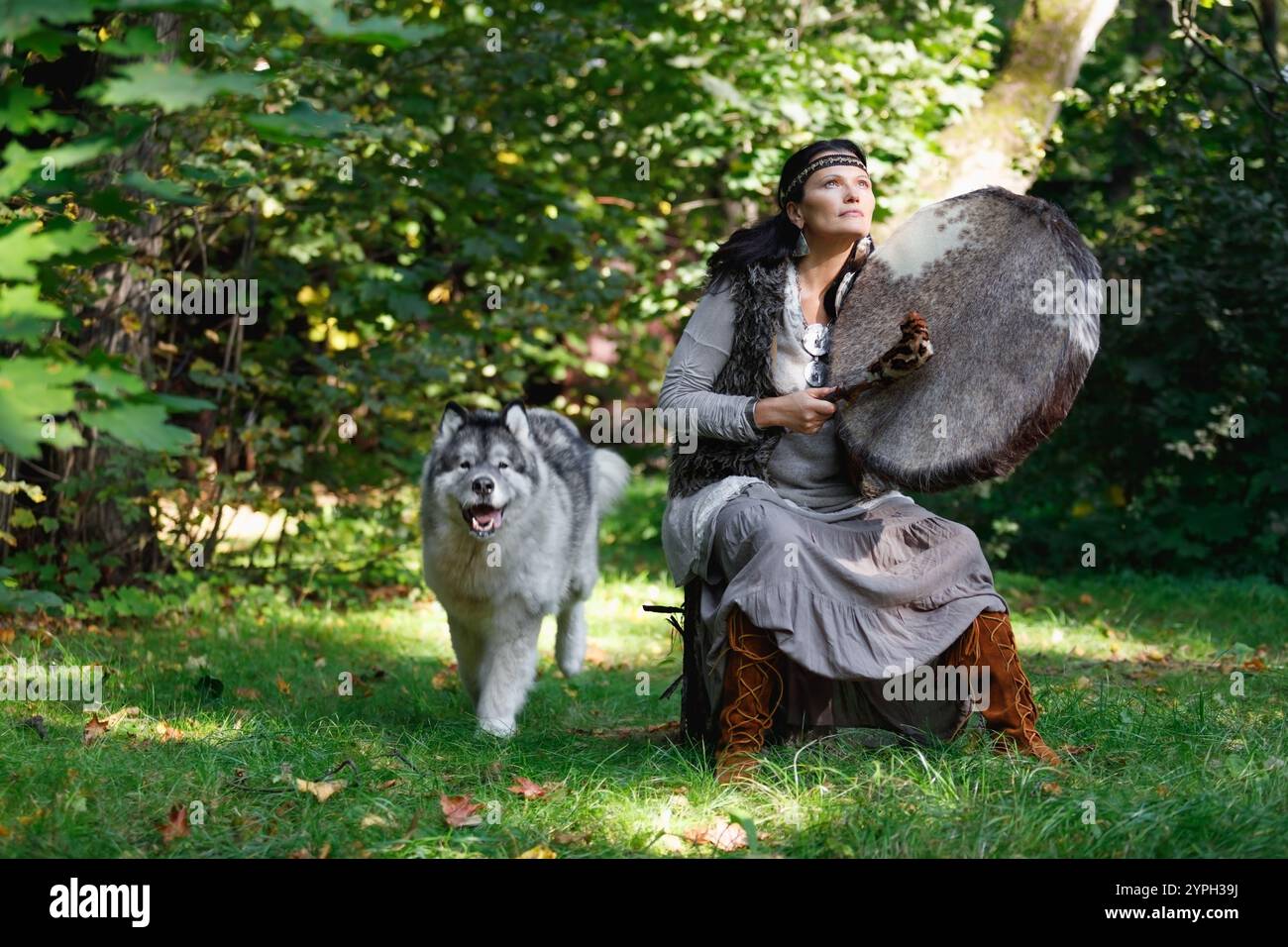 Shaman woman playing her shaman sacred drum in the sunny forest against ...
