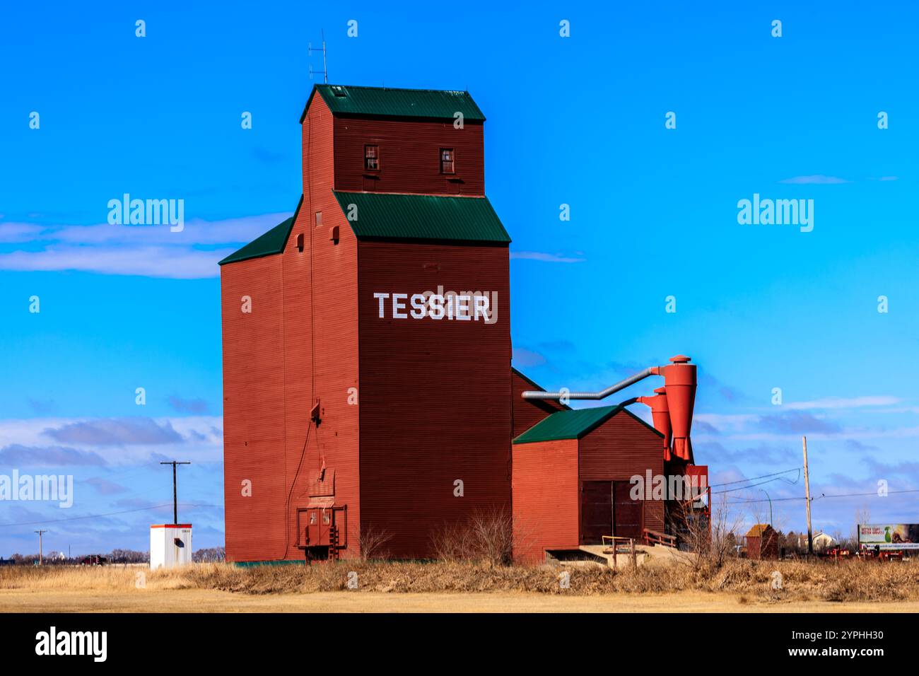 A red and green Tessier grain silo is standing in a field. The sky is ...