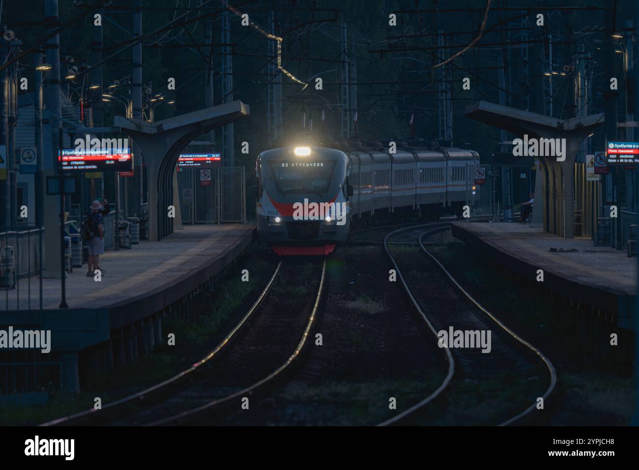 A train approaching a dimly lit station at dusk, with glowing ...