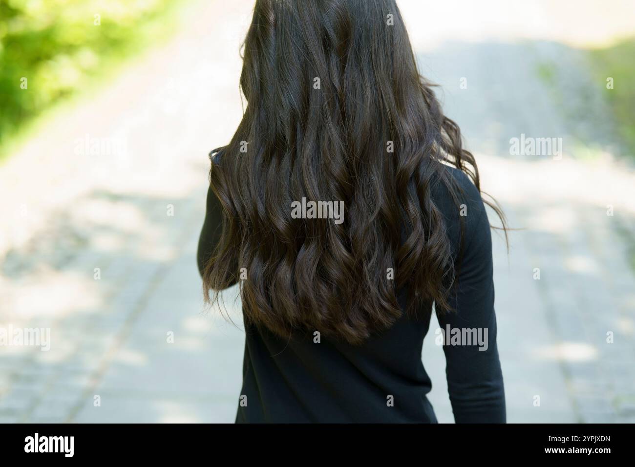 Beautiful girl with long dark curly hair walking along path in summer ...