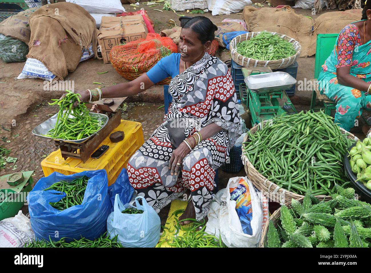Vendor weighing chillis on a set of scales in the vegetable market at Secunderabad, Telegana ...