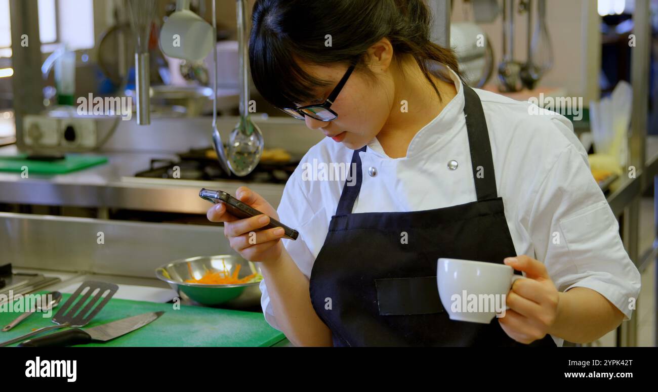 Female chef using mobile phone while having coffee in kitchen Stock ...