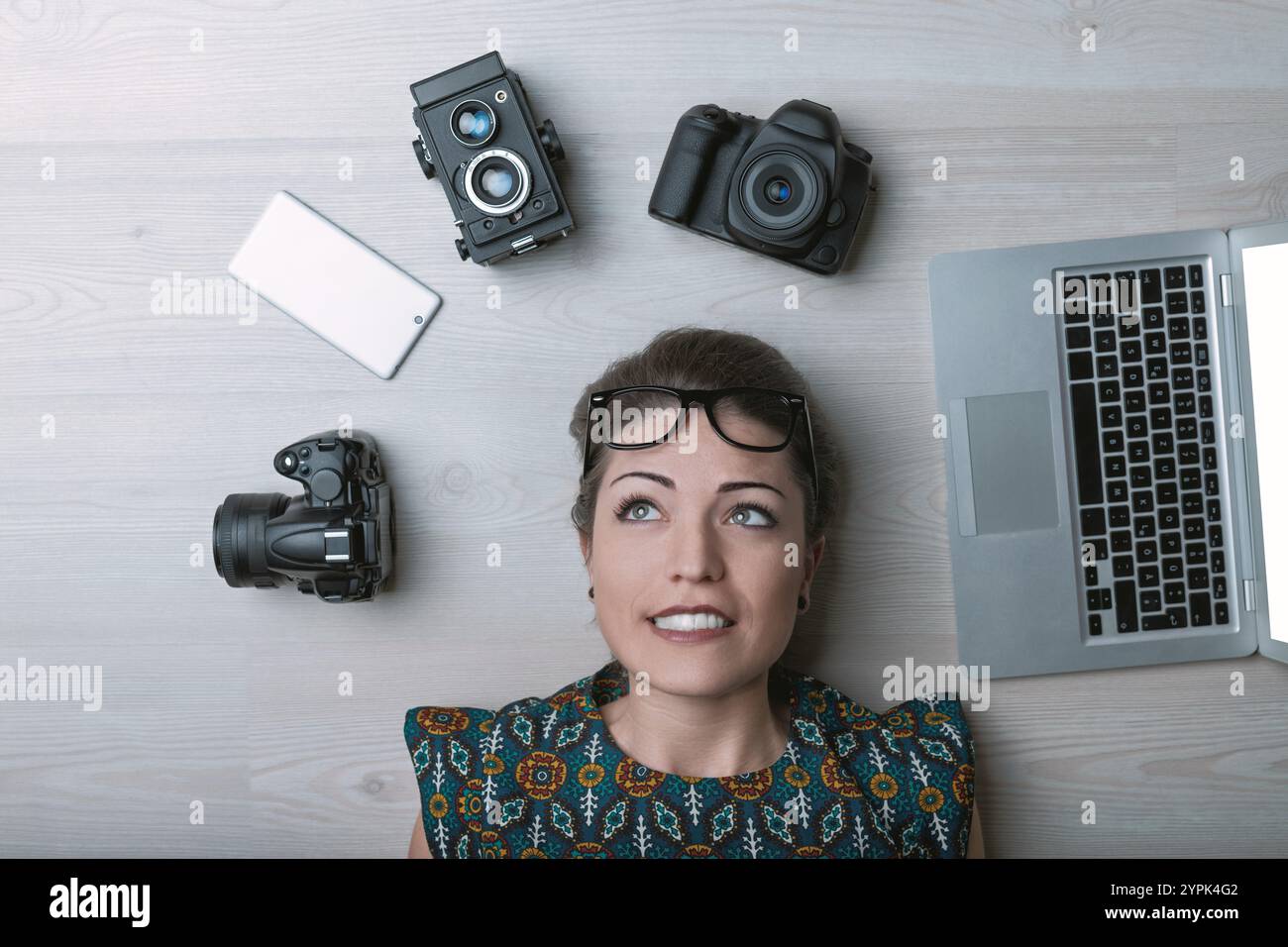 Young smiling photographer is lying on the floor with cameras, laptop ...
