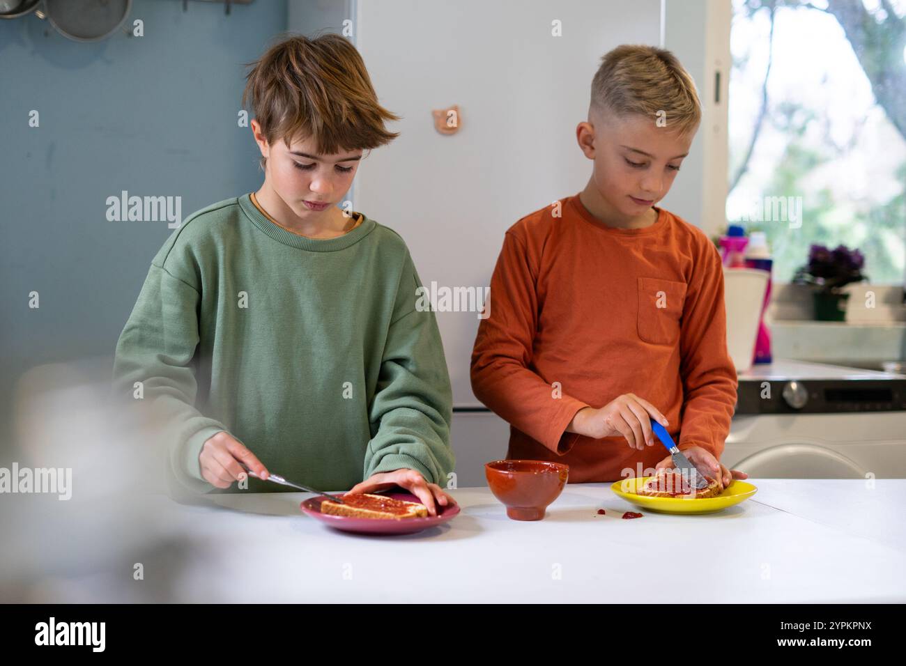 Two Caucasian children spreading jam on toast in the kitchen at home ...