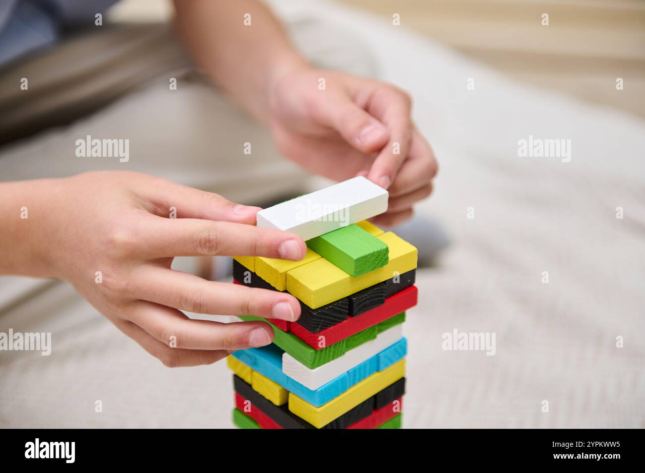 Close-up of hands carefully stacking colorful blocks in a game ...