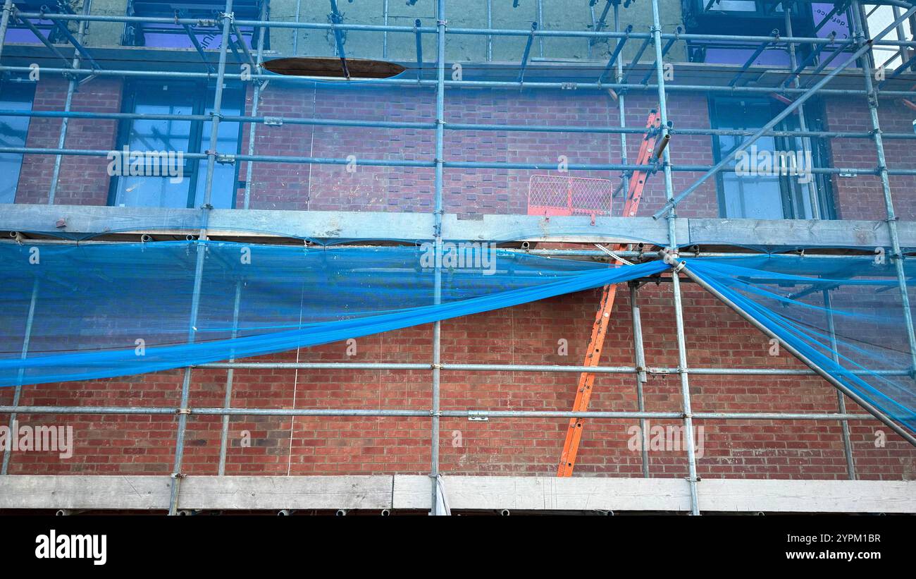 Scaffolding and blue safety netting cover a brick building under ...