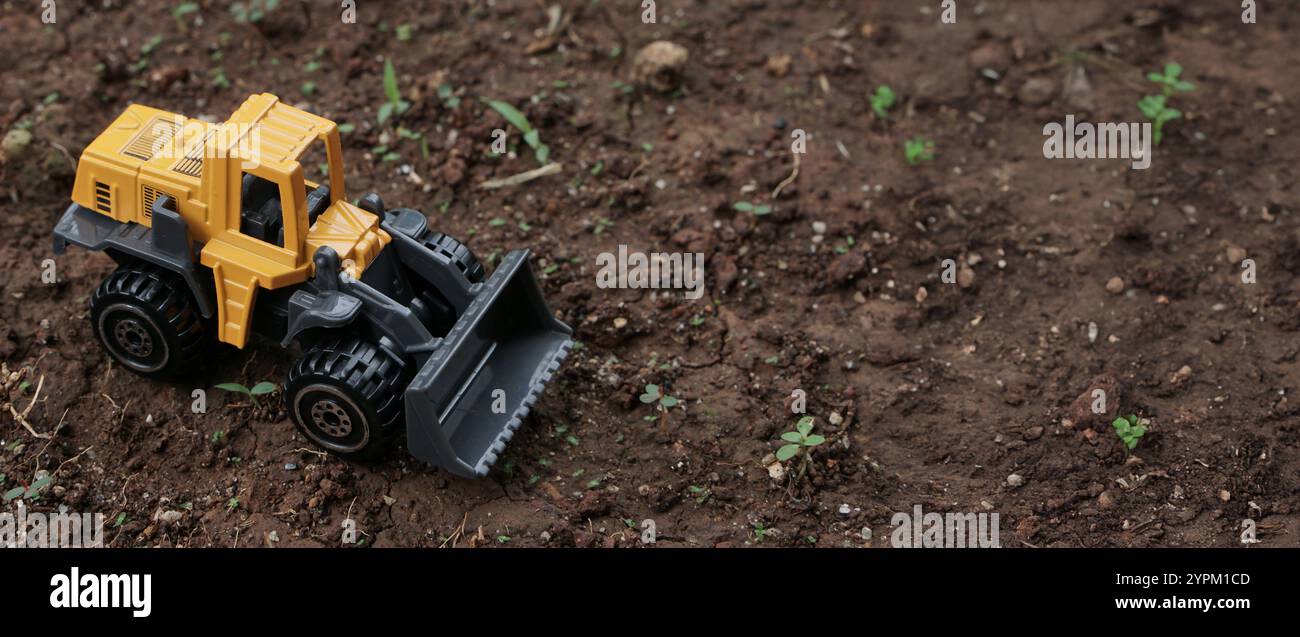Yellow wheel loader or tractor toy on soil or ground background viewed ...