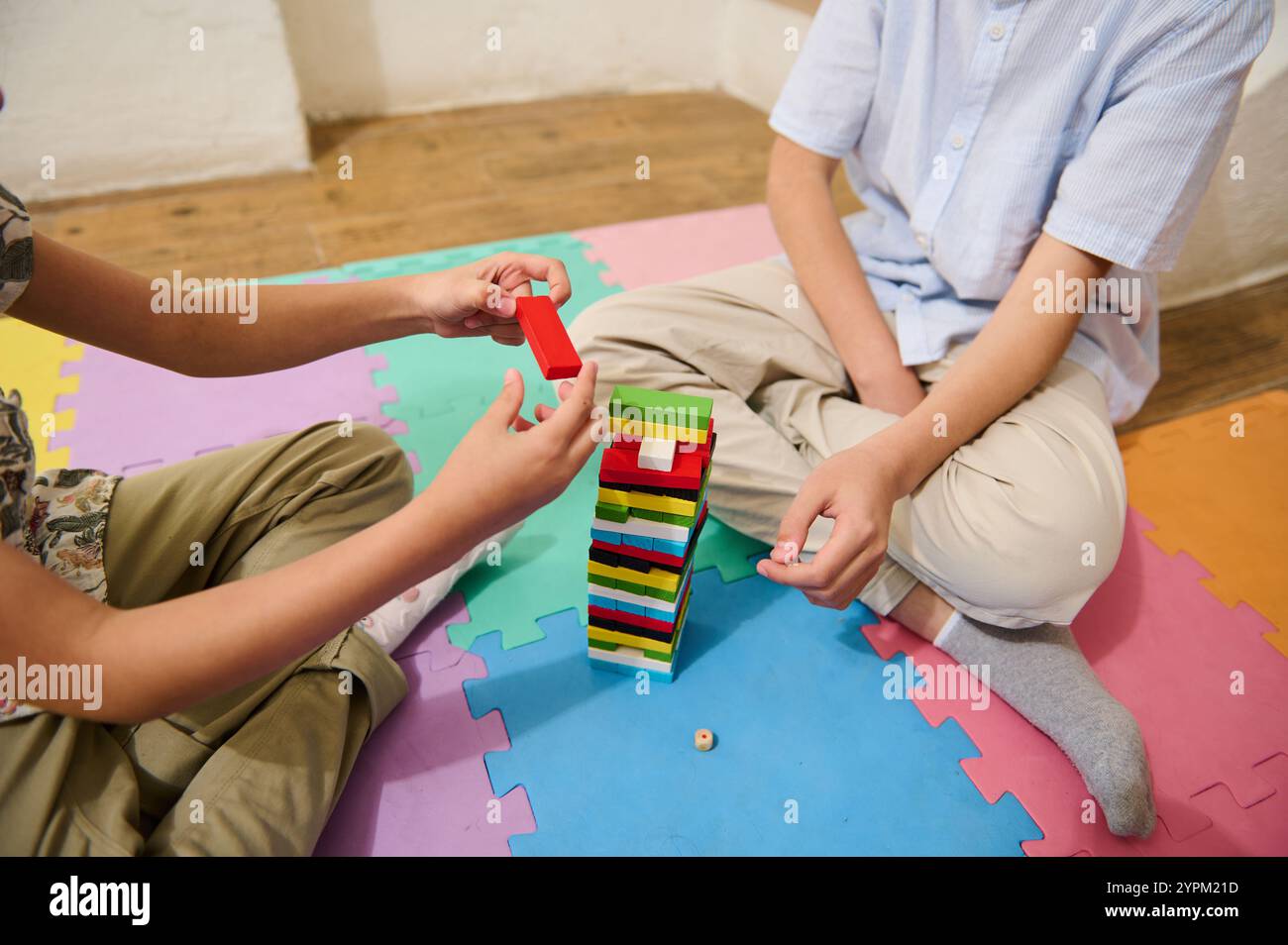 Two children engage in a block stacking game on colorful foam mats ...