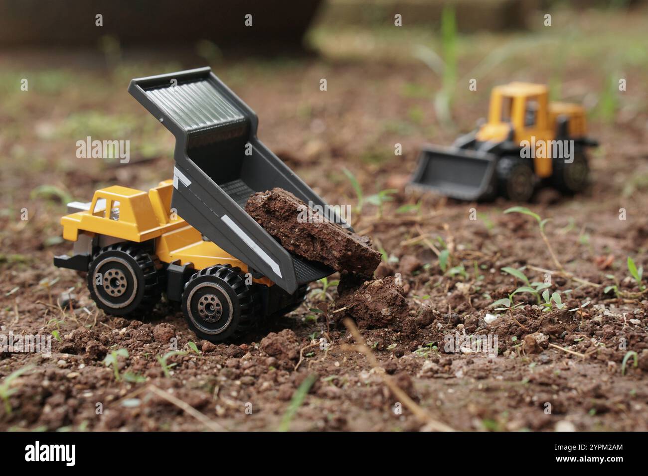 side rear view of yellow small dump truck toy model dumping soil on the ...