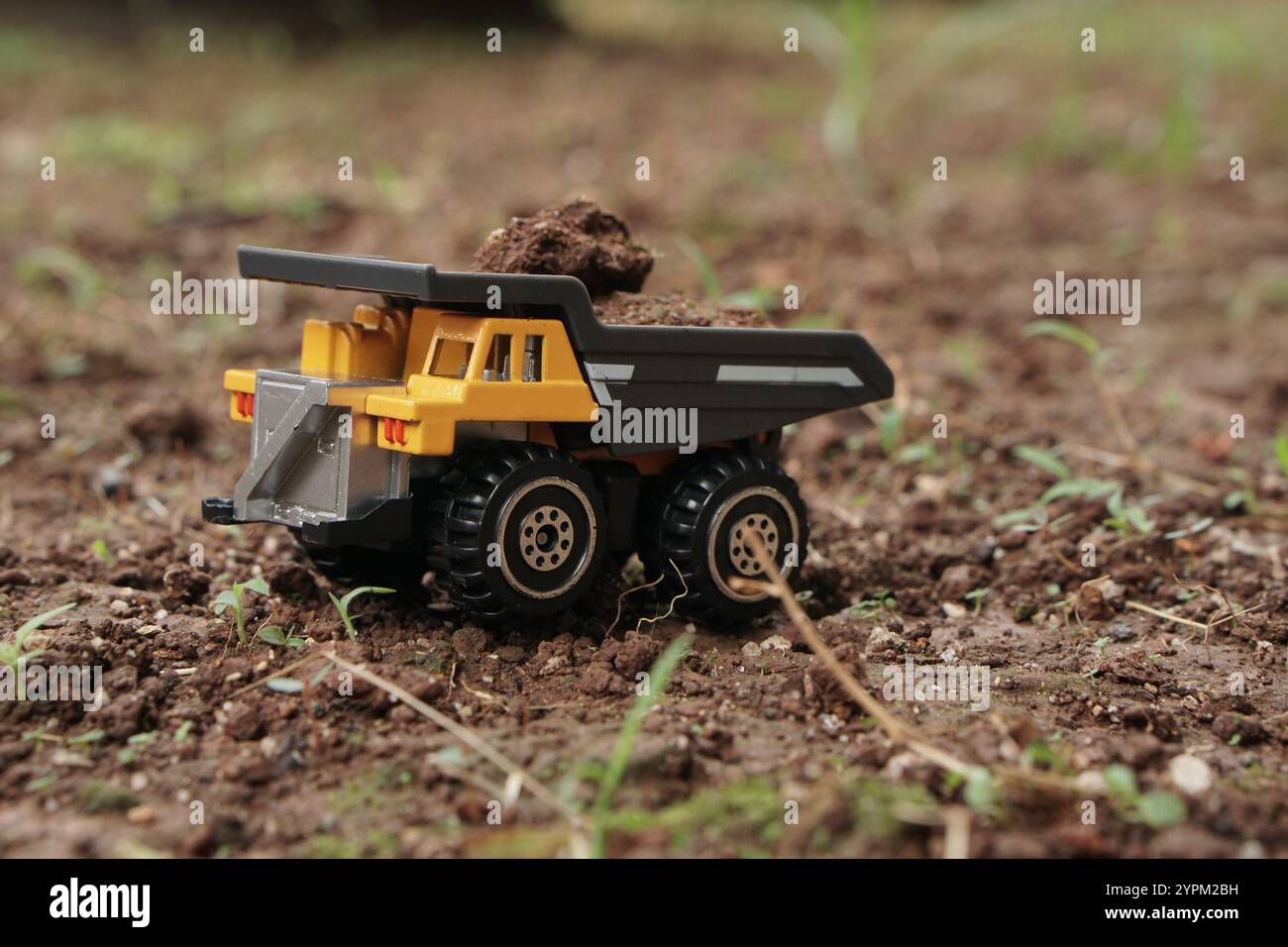 side view of yellow small dump truck toy model transporting soil on the ...