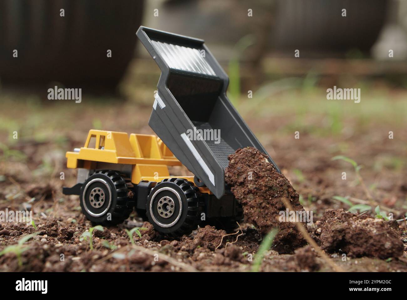side rear view of yellow small dump truck toy model dumping soil on the ...