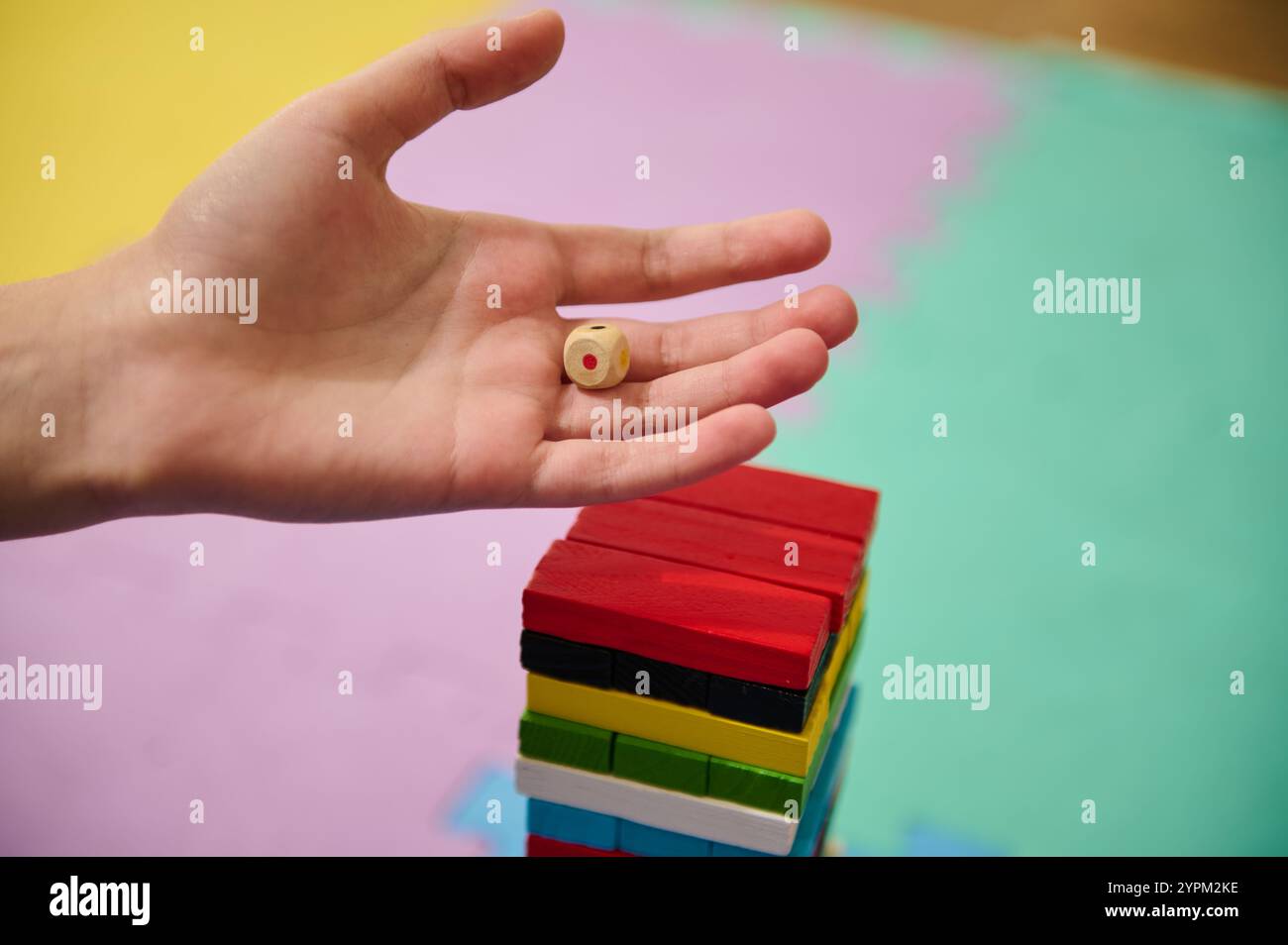 A child's hand holds a small wooden block beside a stack of colorful ...