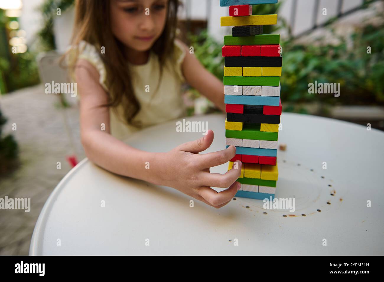 A young girl carefully stacks colorful blocks on a round table while ...