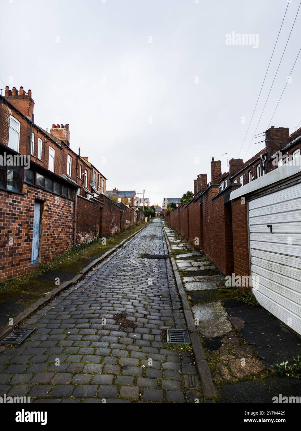 Narrow Cobblestone Alleyway Flanked by Red Brick Houses and Garages on ...