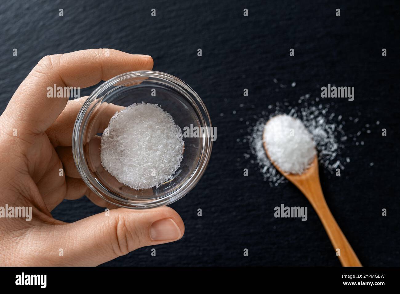 Bowl of monosodium glutamate in woman fingers over black background ...