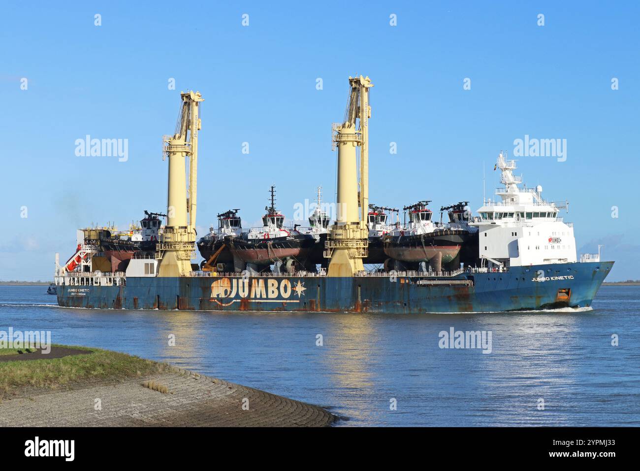 a heavy load carrier with tug boats and cranes is navigating through ...