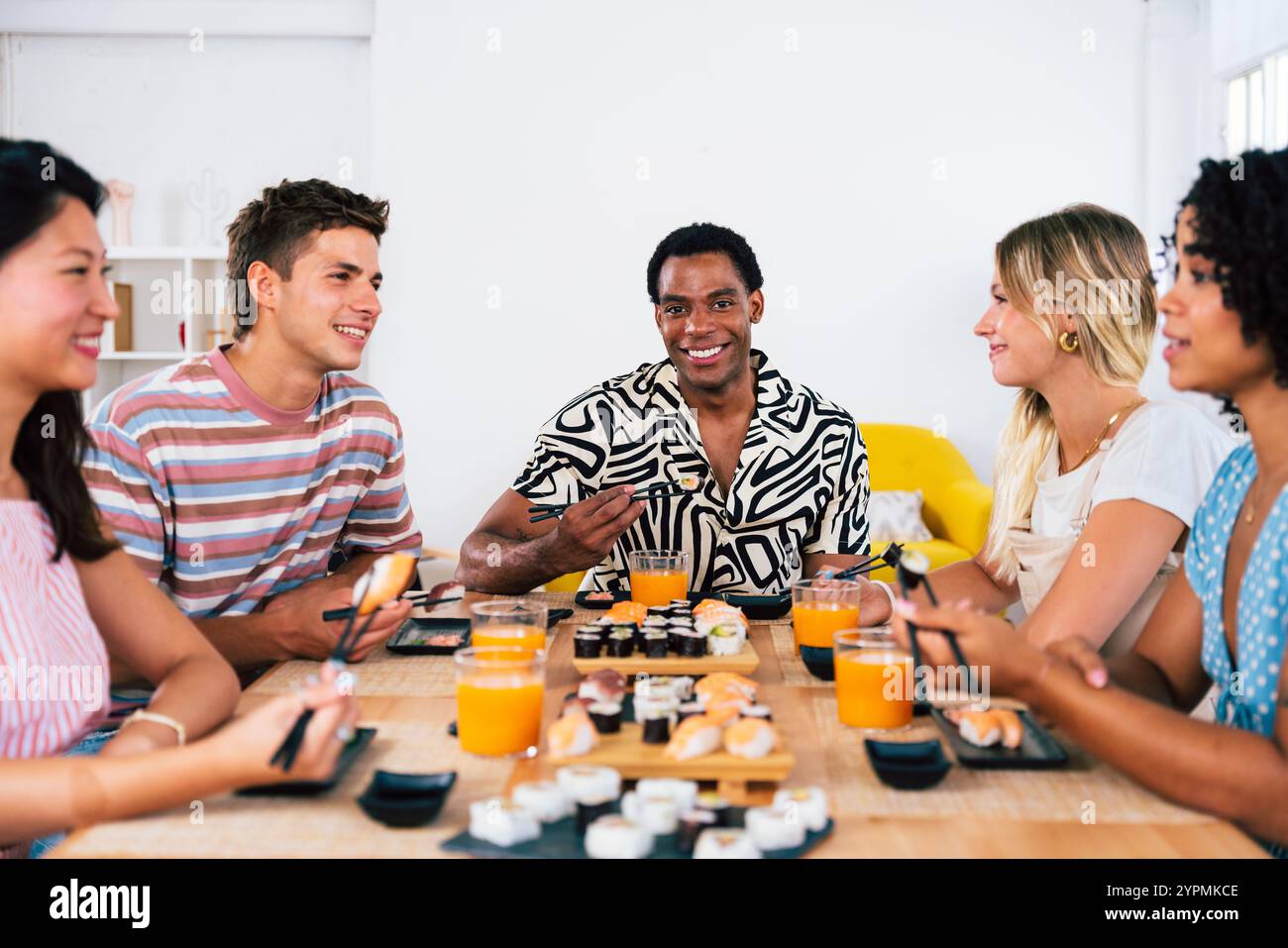 Multiethnic group of young friends meeting at home and eating sushi ...