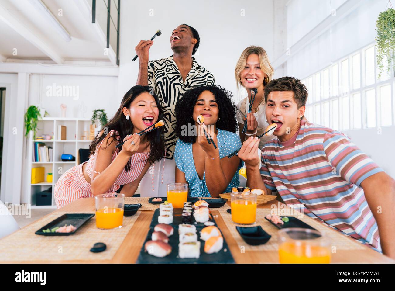 Multiethnic group of young friends meeting at home and eating sushi ...