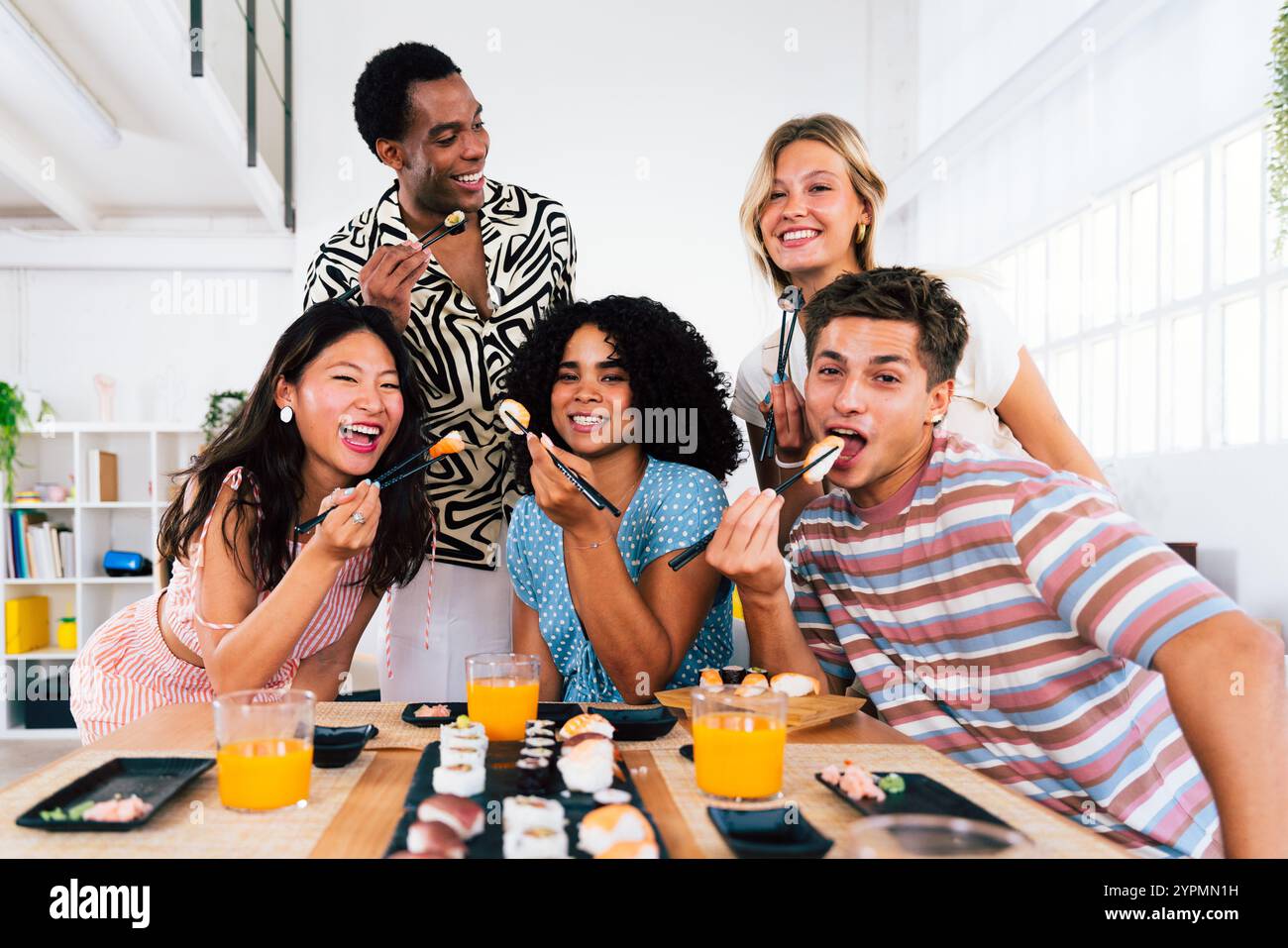 Multiethnic group of young friends meeting at home and eating sushi ...