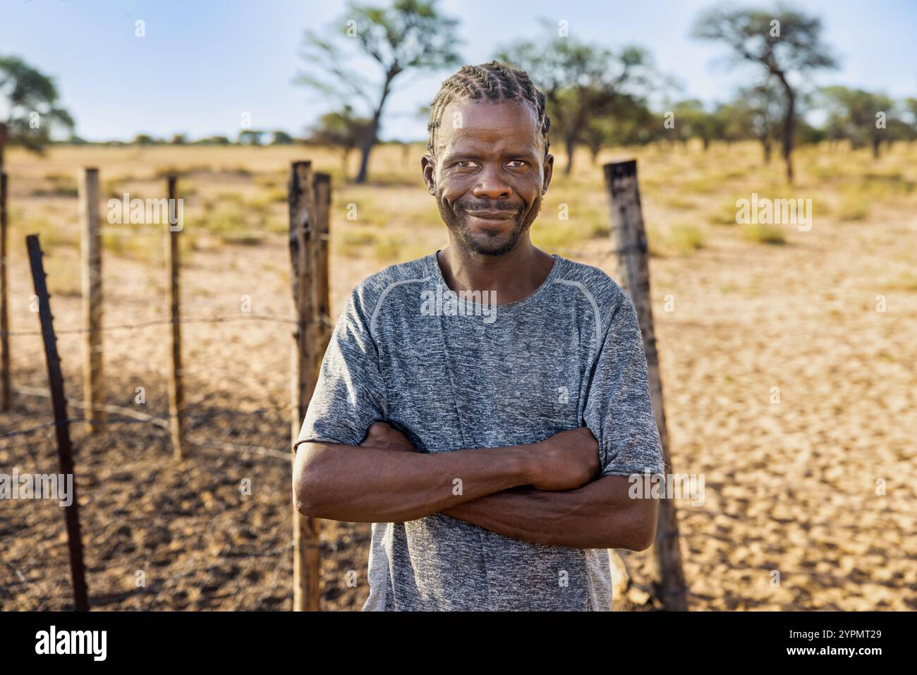 village african man with braids, standing in the yard in front of fence ...