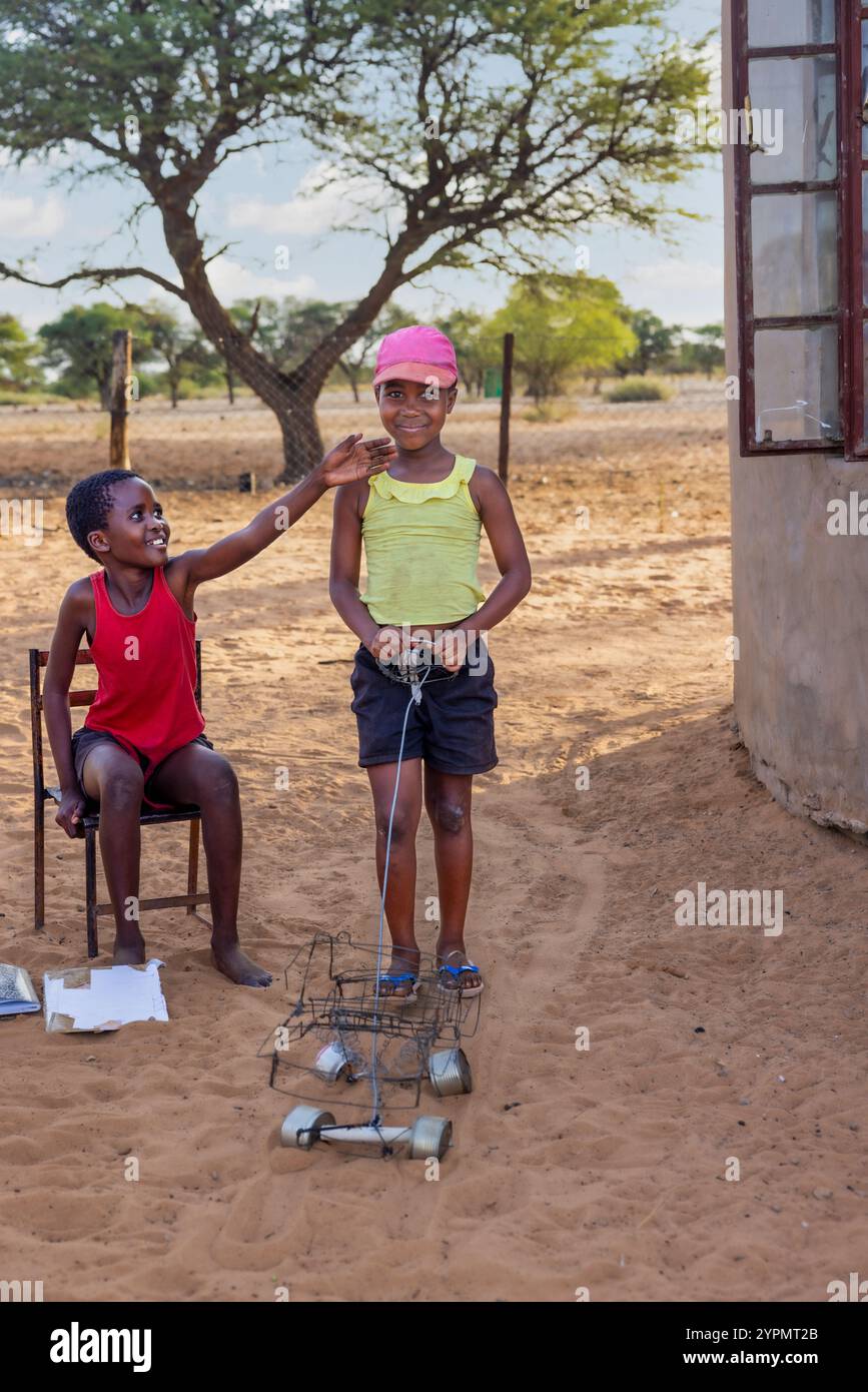 village african girls children playing with a wire car toy in the yard ...