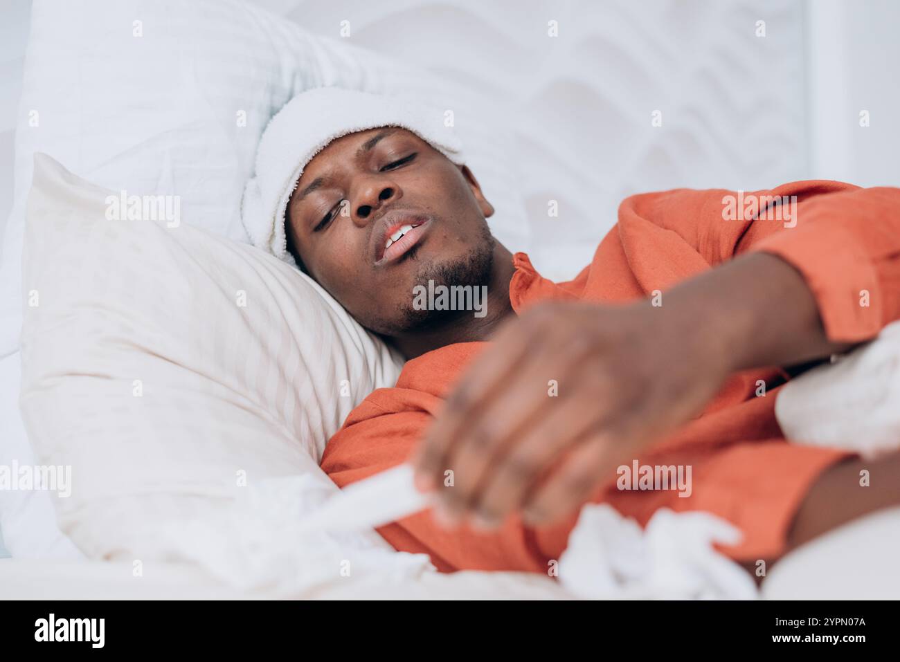 Sick black man lies in bed with a compress on his forehead. Holding a ...