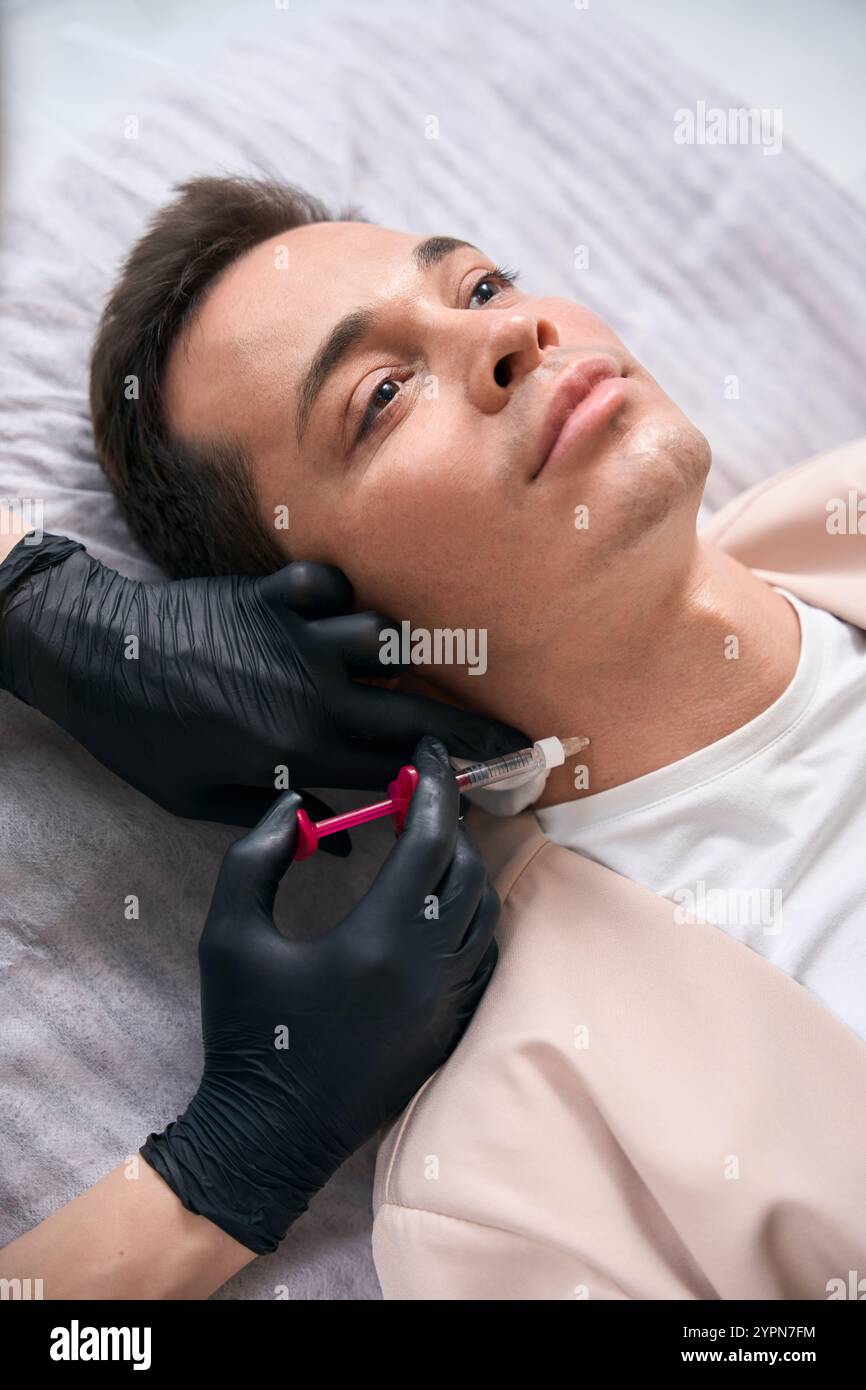 Adult man undergoing filler injections into neck lying on the treatment ...
