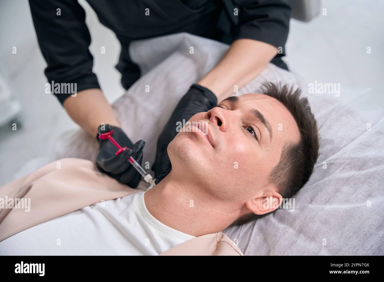 Focused state-licensed beautician making injections of filler into male ...