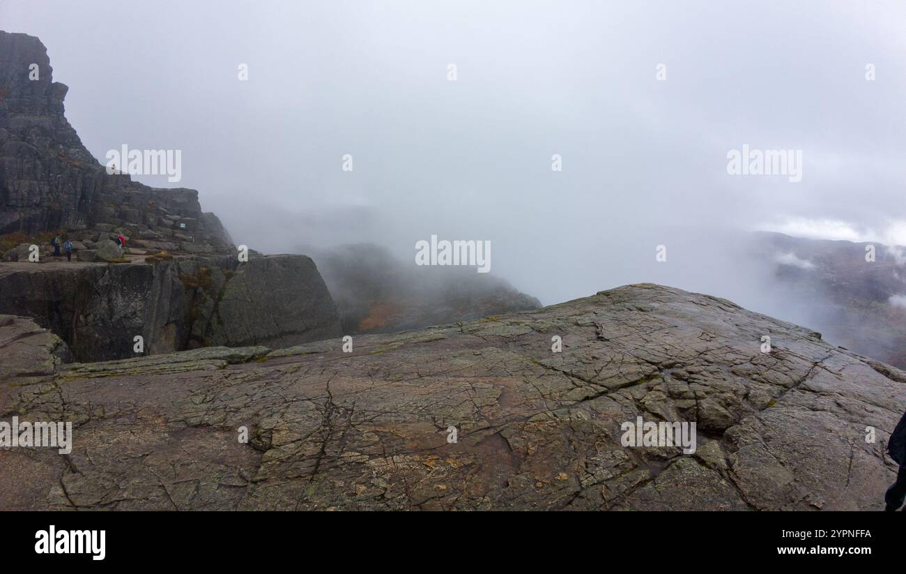 A rocky landscape shrouded in fog, with a rugged cliff on the left and ...