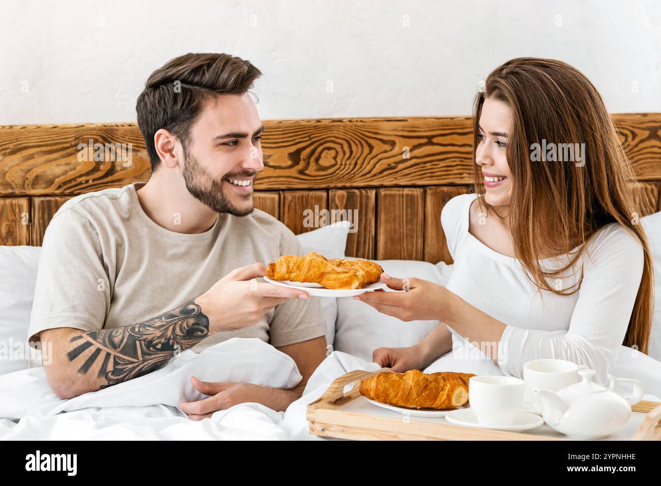Romantic breakfast for two concept. Girl gives croissant to man, in bed ...