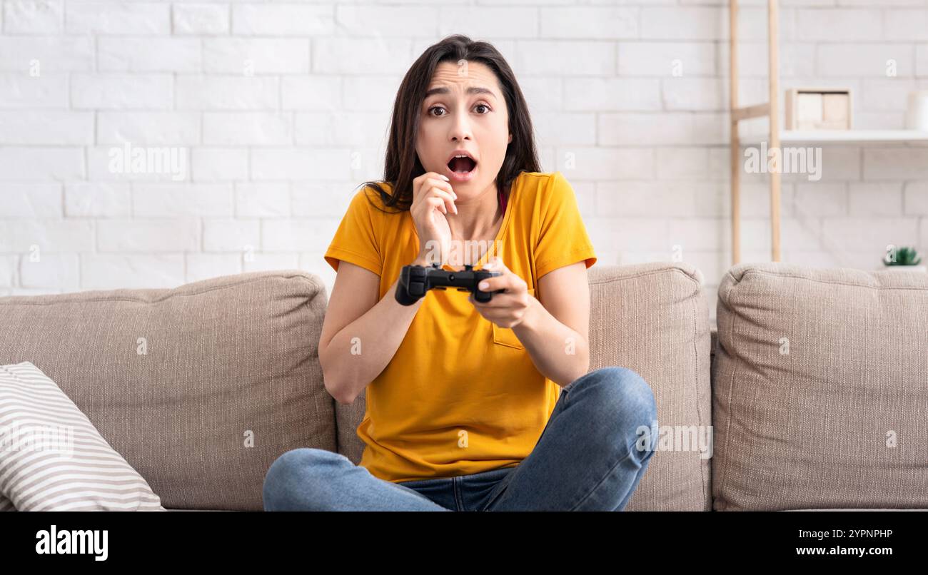 Emotional millennial girl with console playing video games on cozy sofa ...