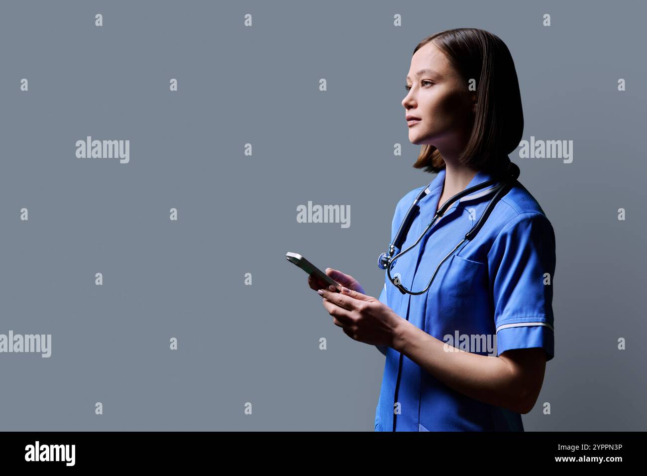 Female nurse using smartphone, profile view on gray studio background ...