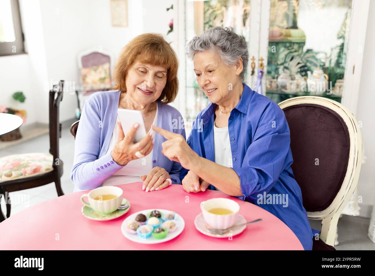 Elderly women enjoying a friendly conversation over tea and sweets at a ...