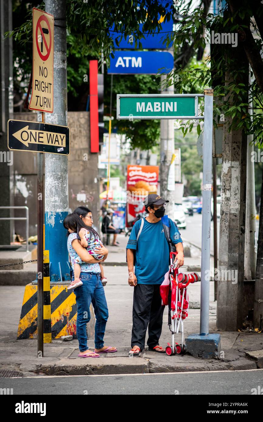A young Filipino family pause to cross the Mabini road in the busy ...
