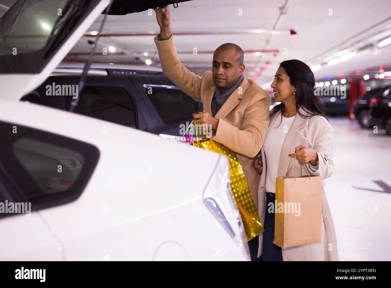 Married couple loading gift bags into trunk of car in an underground ...