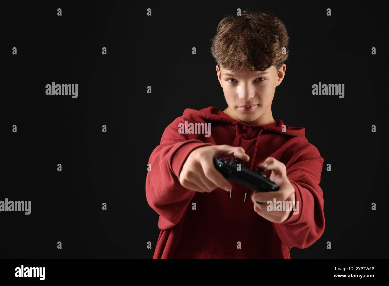 Teenage boy playing video game with controller on black background ...