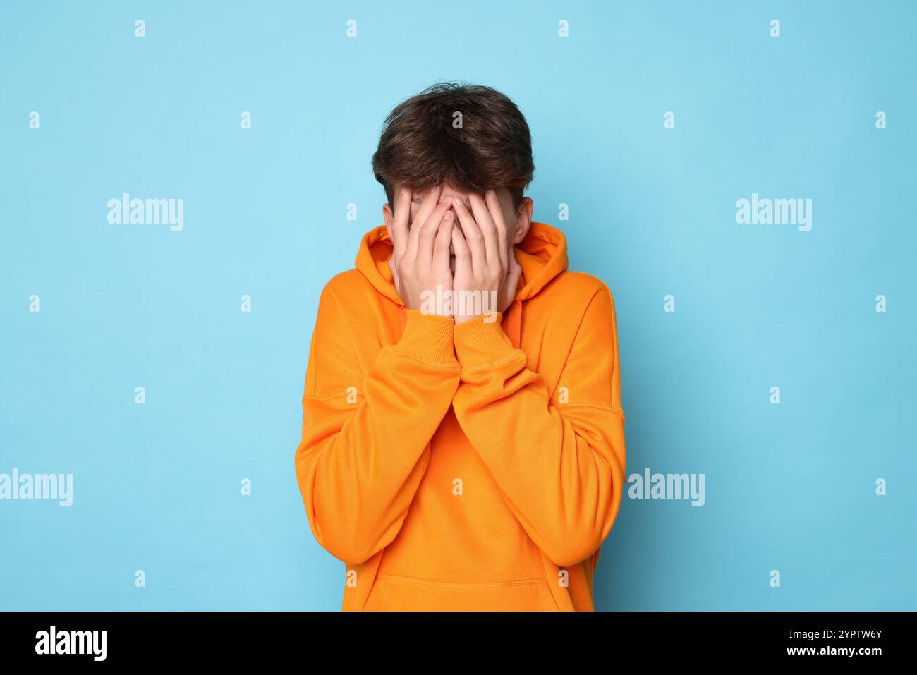 Scared teenage boy covering face with hands on light blue background ...