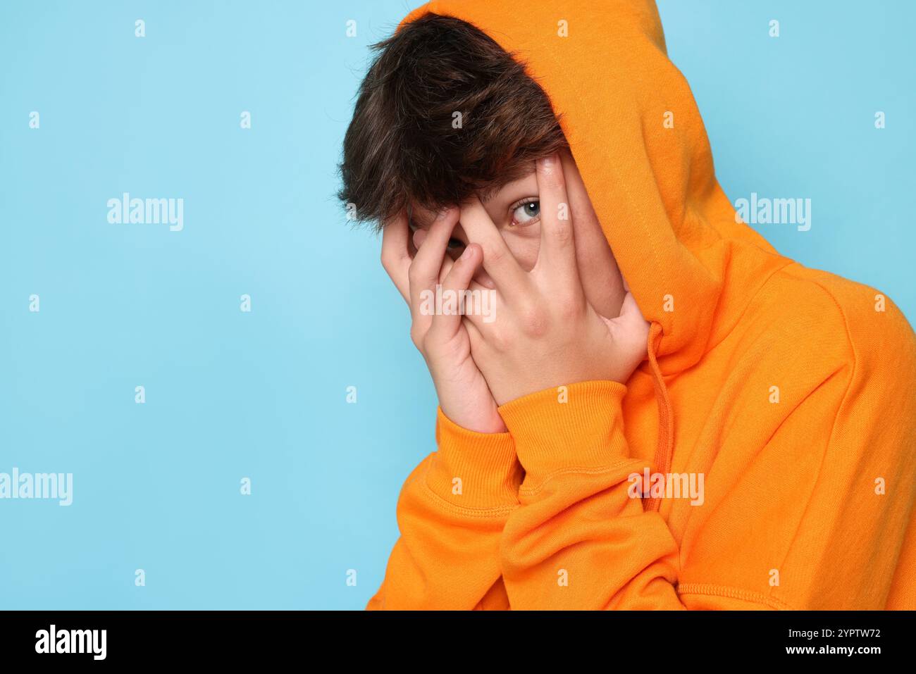 Scared teenage boy covering face with hands on light blue background ...
