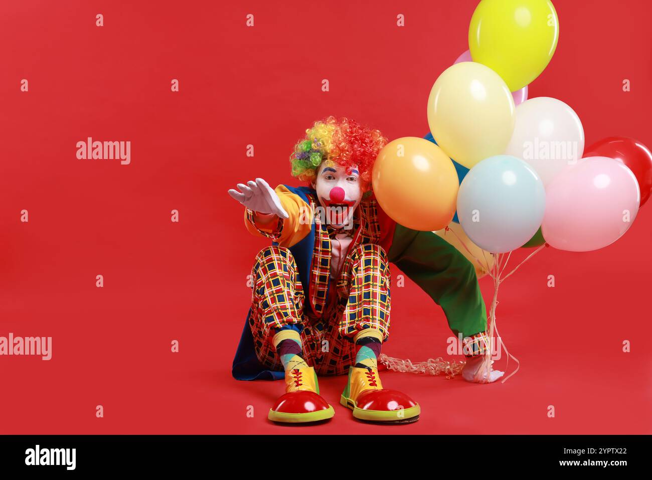Emotional clown with colorful balloons on red background, space for ...