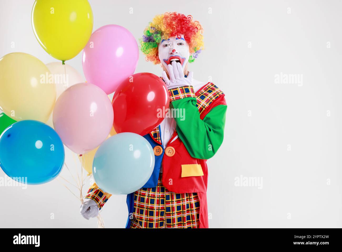 Emotional clown with colorful balloons on light background, space for ...