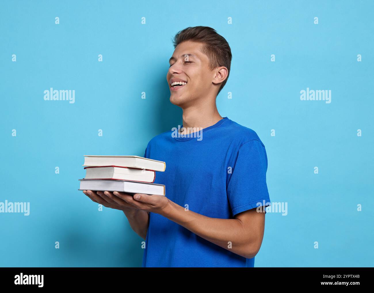 Happy student with stack of books on light blue background Stock Photo ...