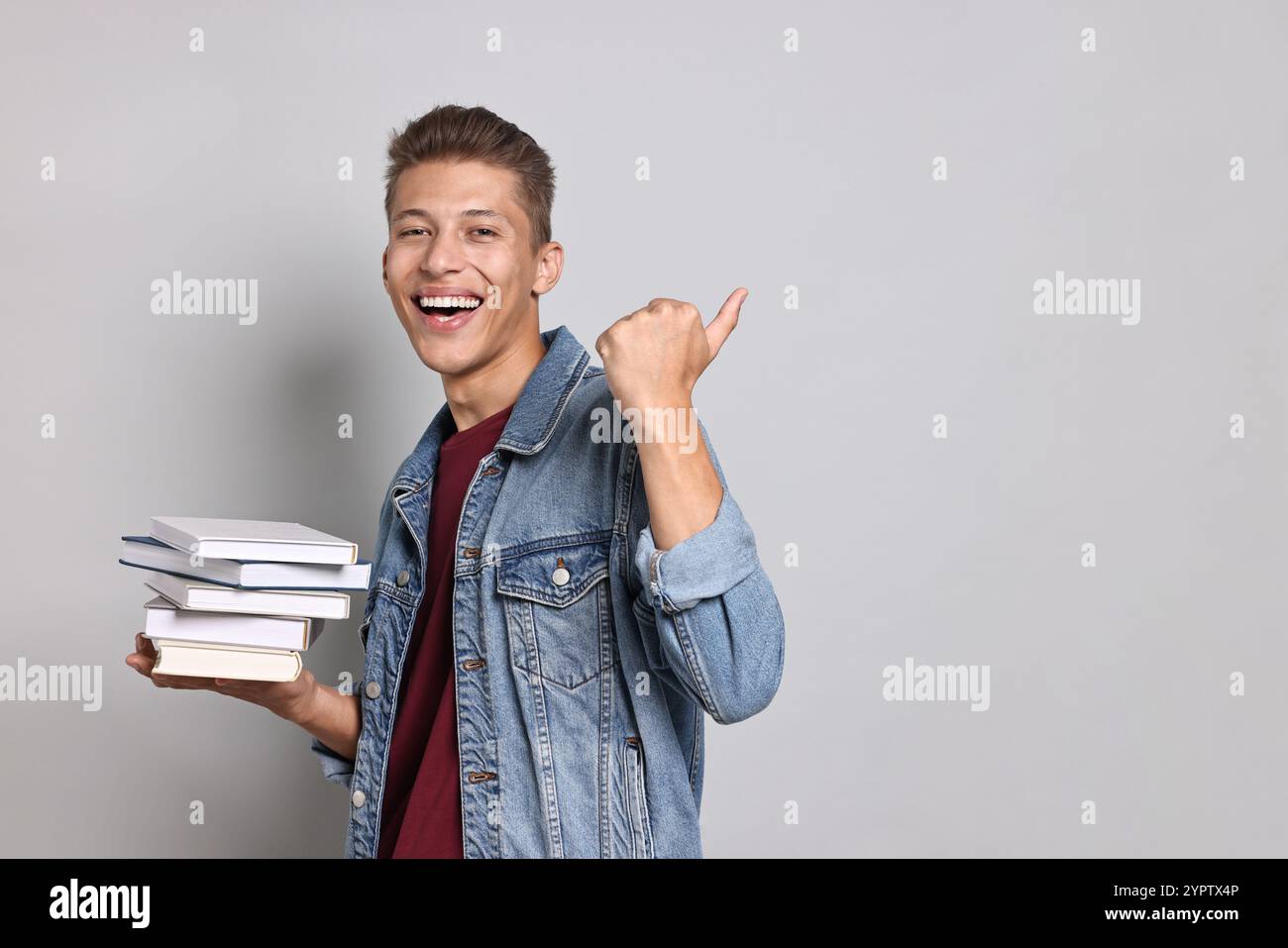 Happy student with stack of books showing thumbs up on grey background ...