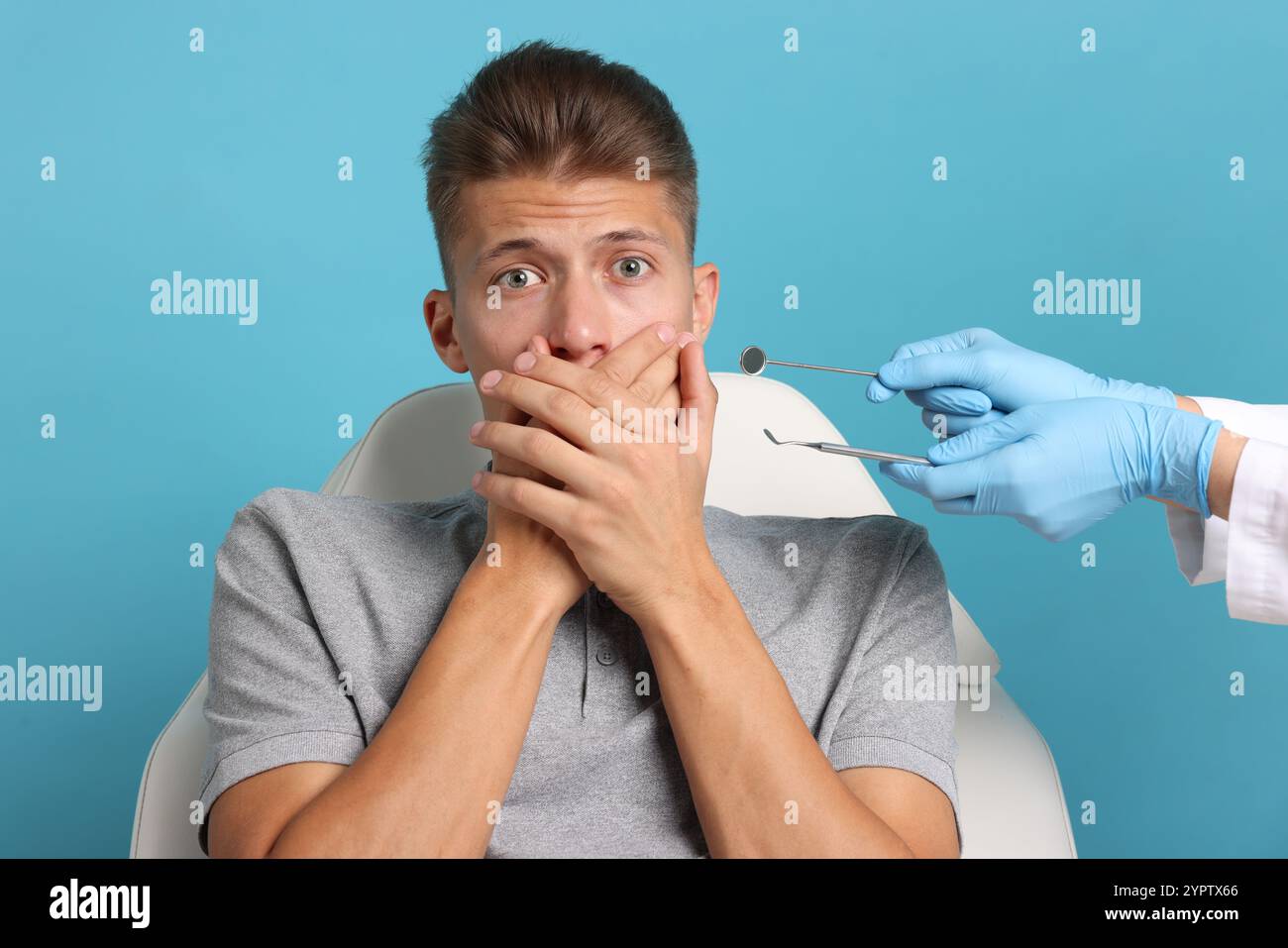 Dental phobia. Dentist working with scared man on light blue background ...
