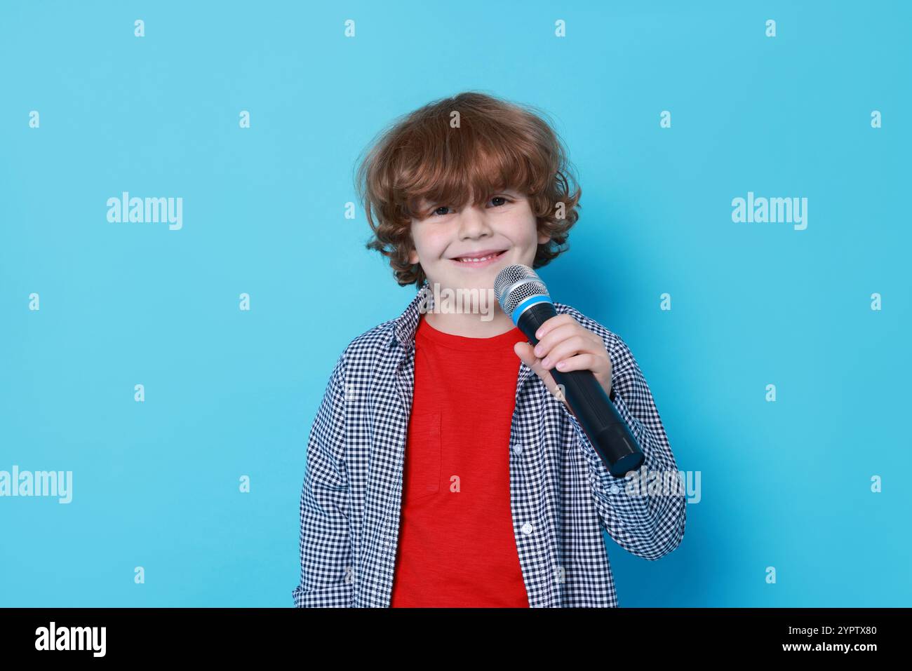 Little boy with microphone pretending to be singer on light blue ...