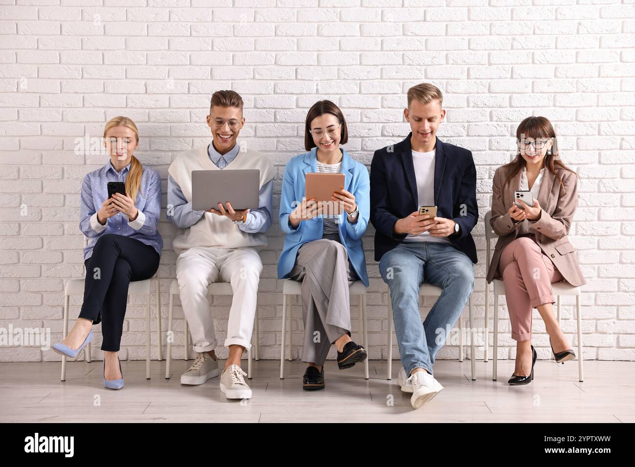 Group of people using different gadgets on chairs near white brick wall ...