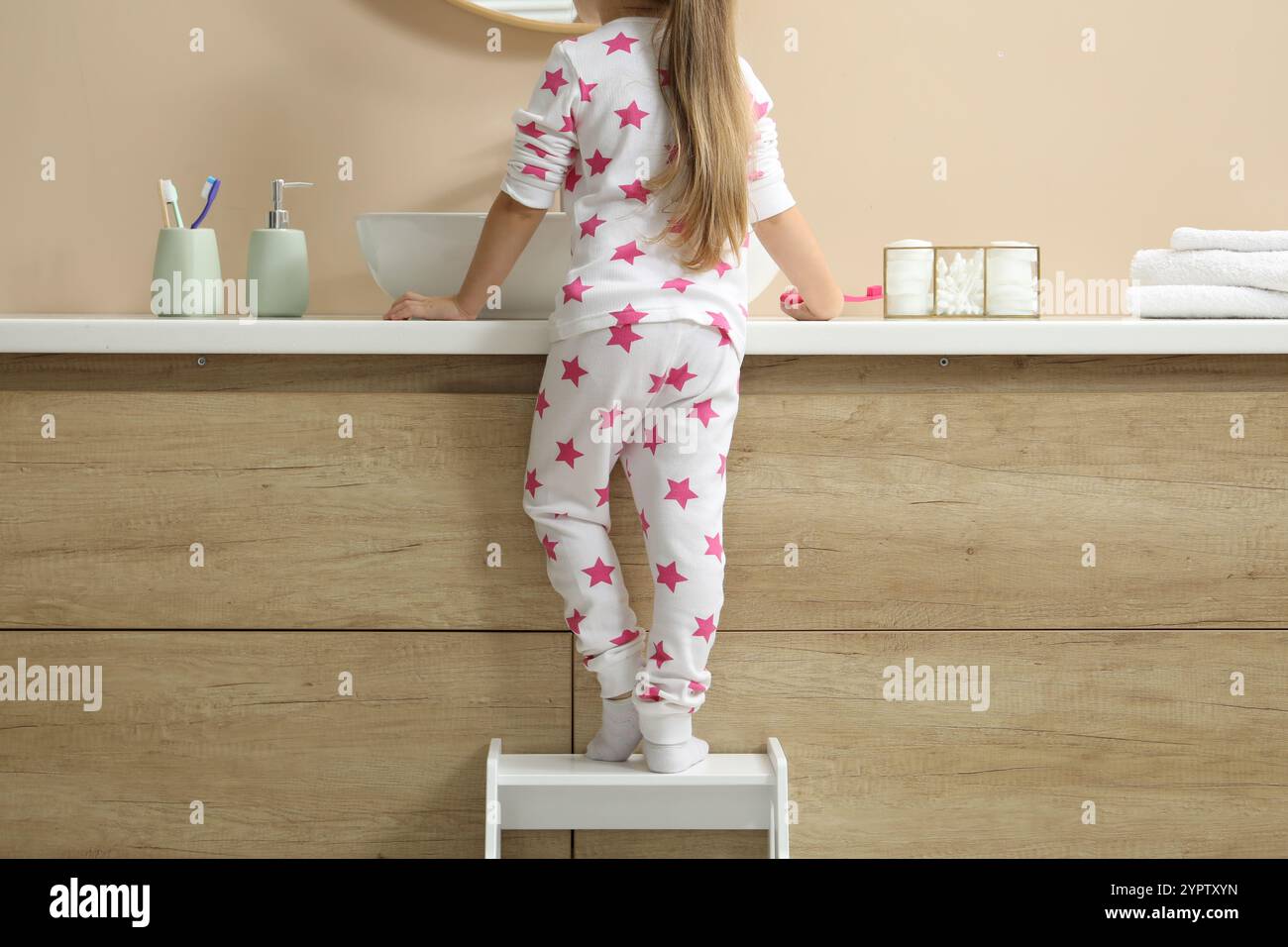 Little girl with toothbrush standing on step stool near bathroom vanity ...