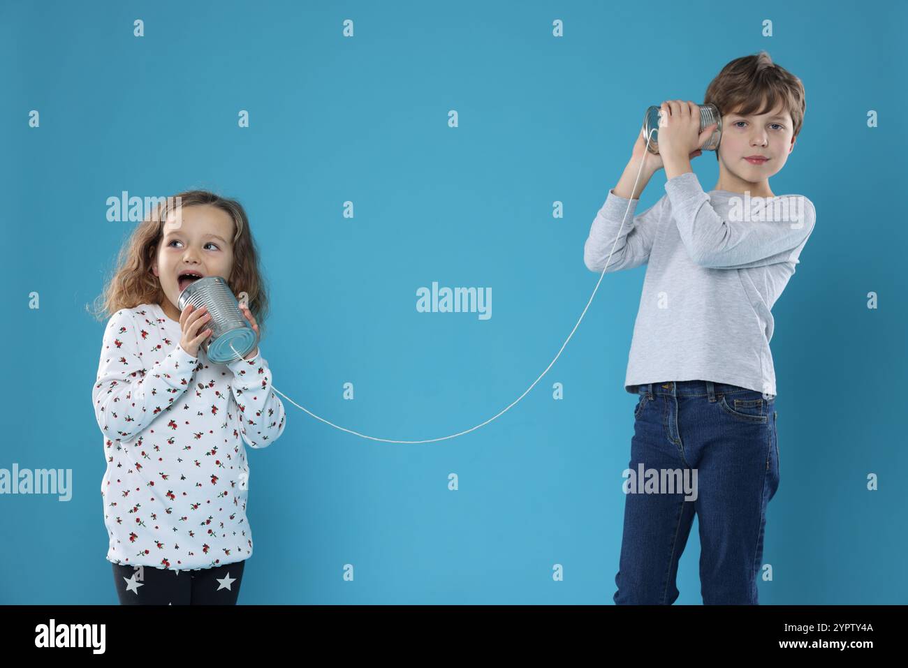 Boy and girl talking on tin can telephone against blue background Stock ...