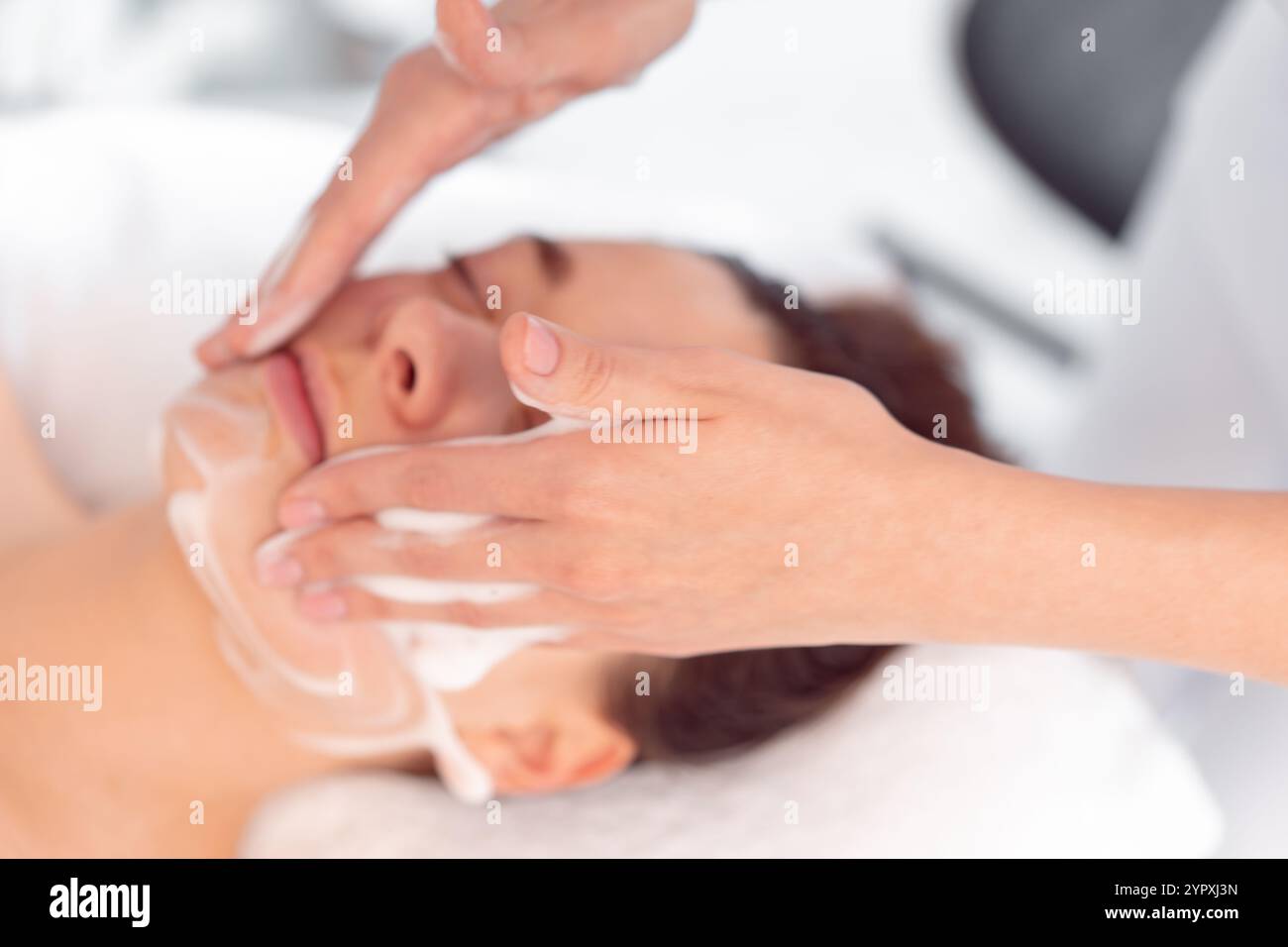 Crop anonymous cosmetologist massaging woman's face at beauty salon ...