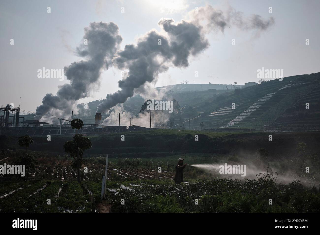 A farmer tends to a field as steam rises from a geothermal power plant ...