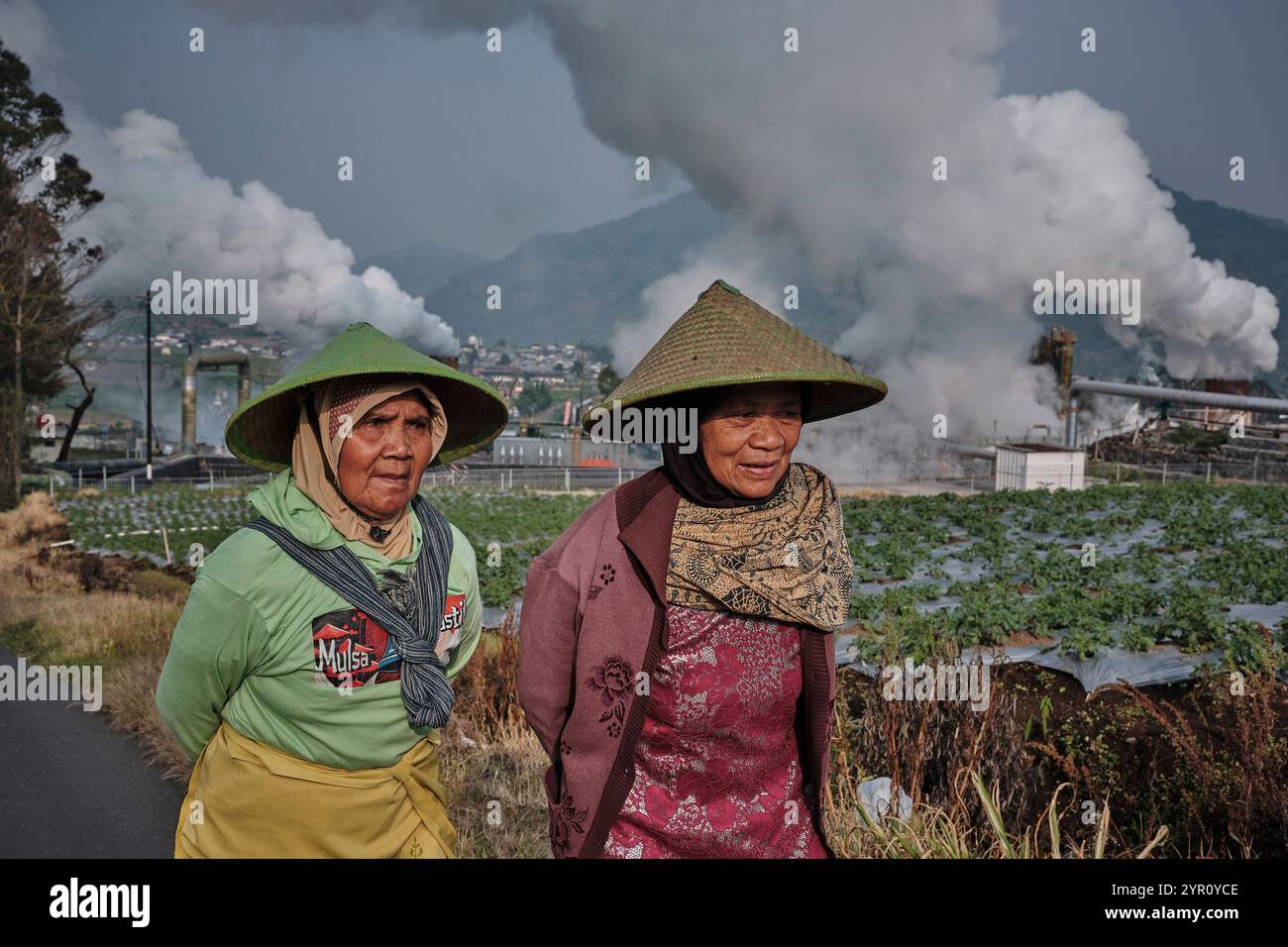 Farmers walk by as steam rises from a geothermal power plant in Dieng ...